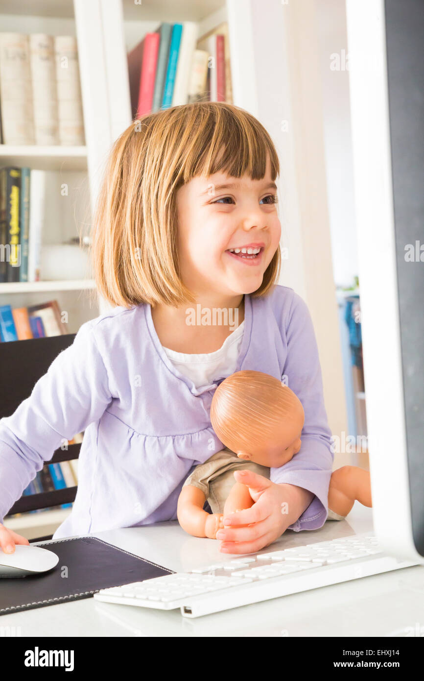 Portrait ofsmiling little girl with doll spending time at computer ...