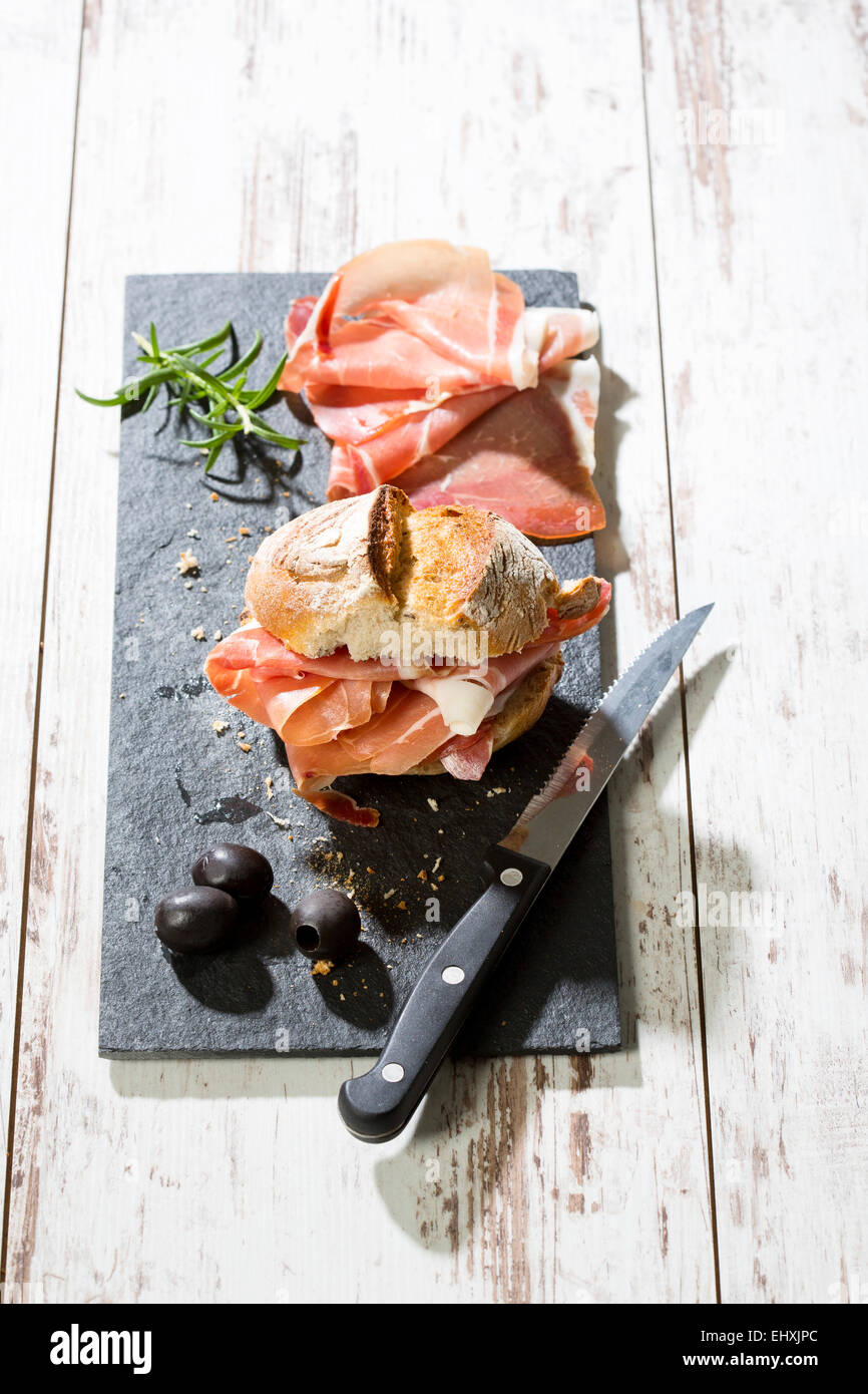 Parma ham, rolls, black olives and knife on chopping board Stock Photo ...