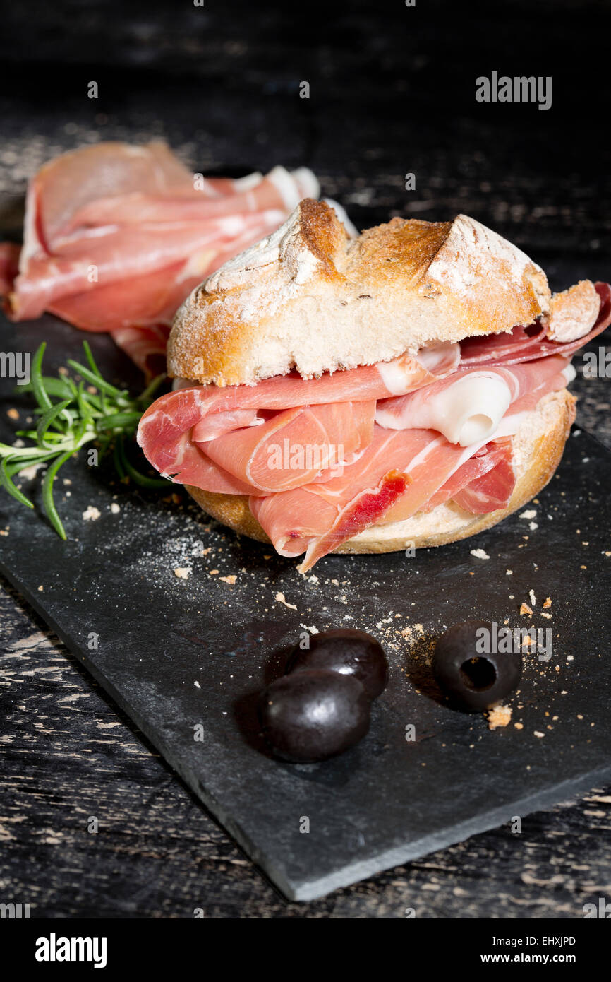 Parma ham, rolls and black olives on dark wood Stock Photo - Alamy