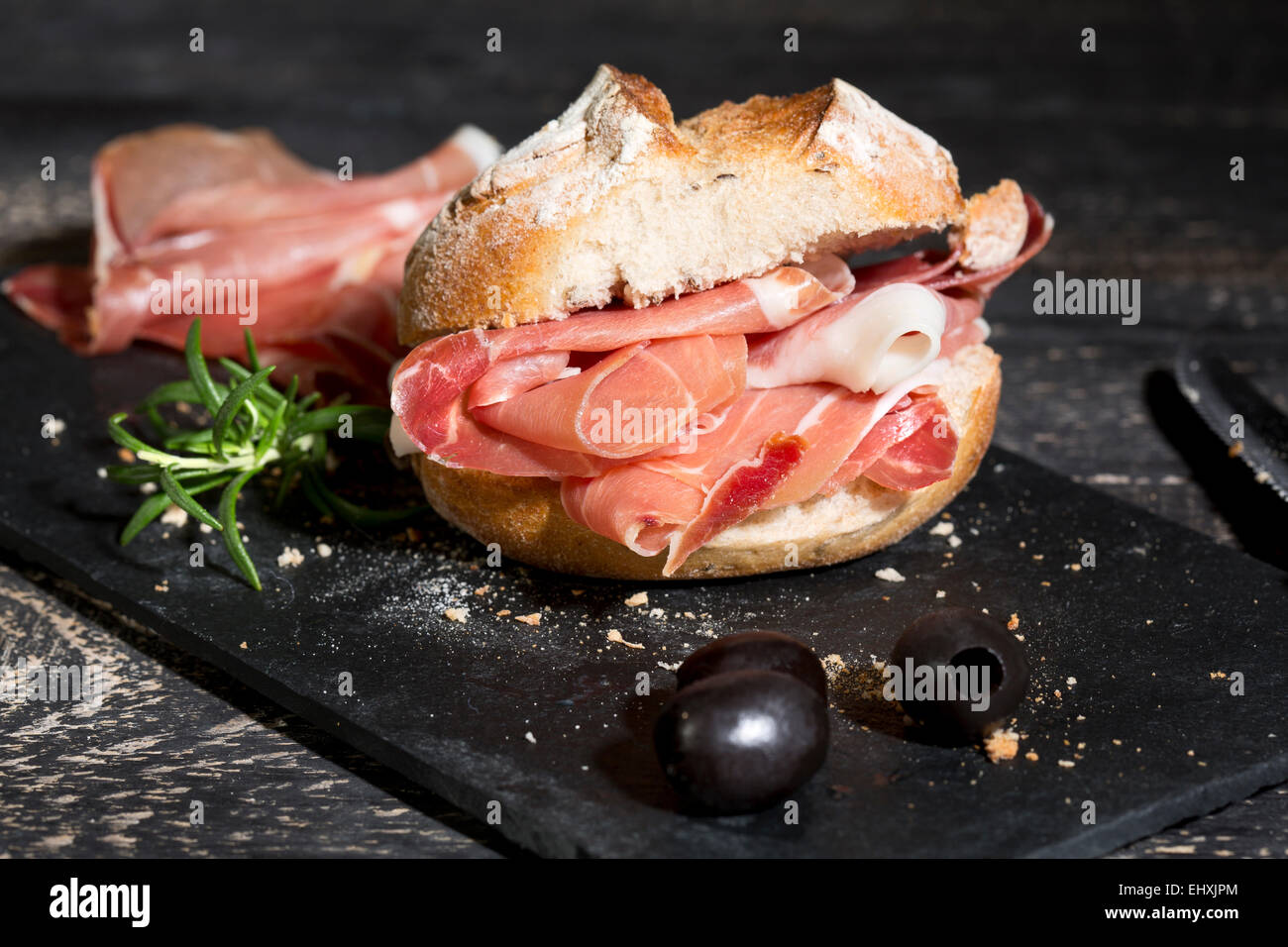 Parma ham, rolls and black olives on dark wood Stock Photo - Alamy