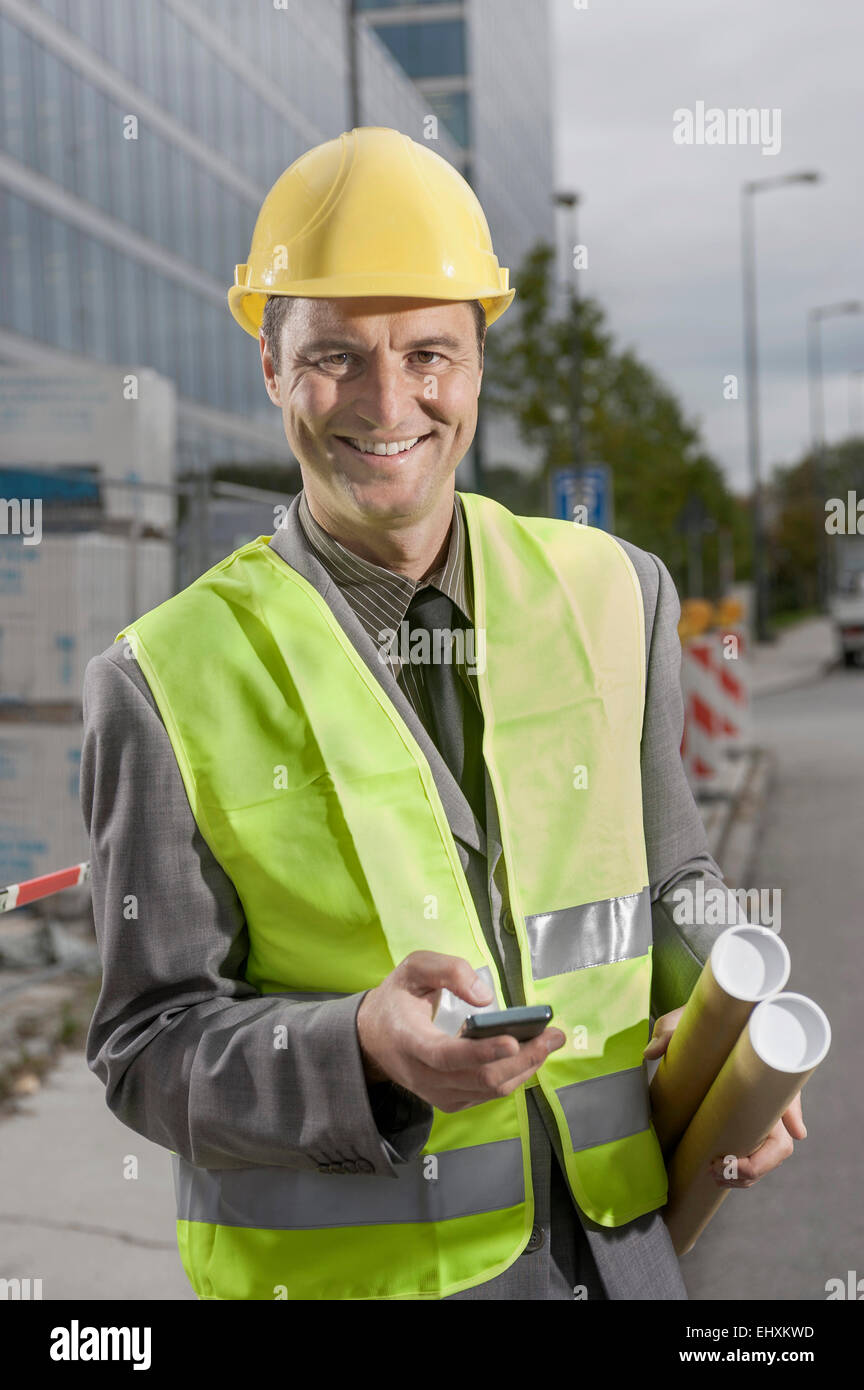 Portrait of a happy site manager holding blueprints and mobile Stock ...