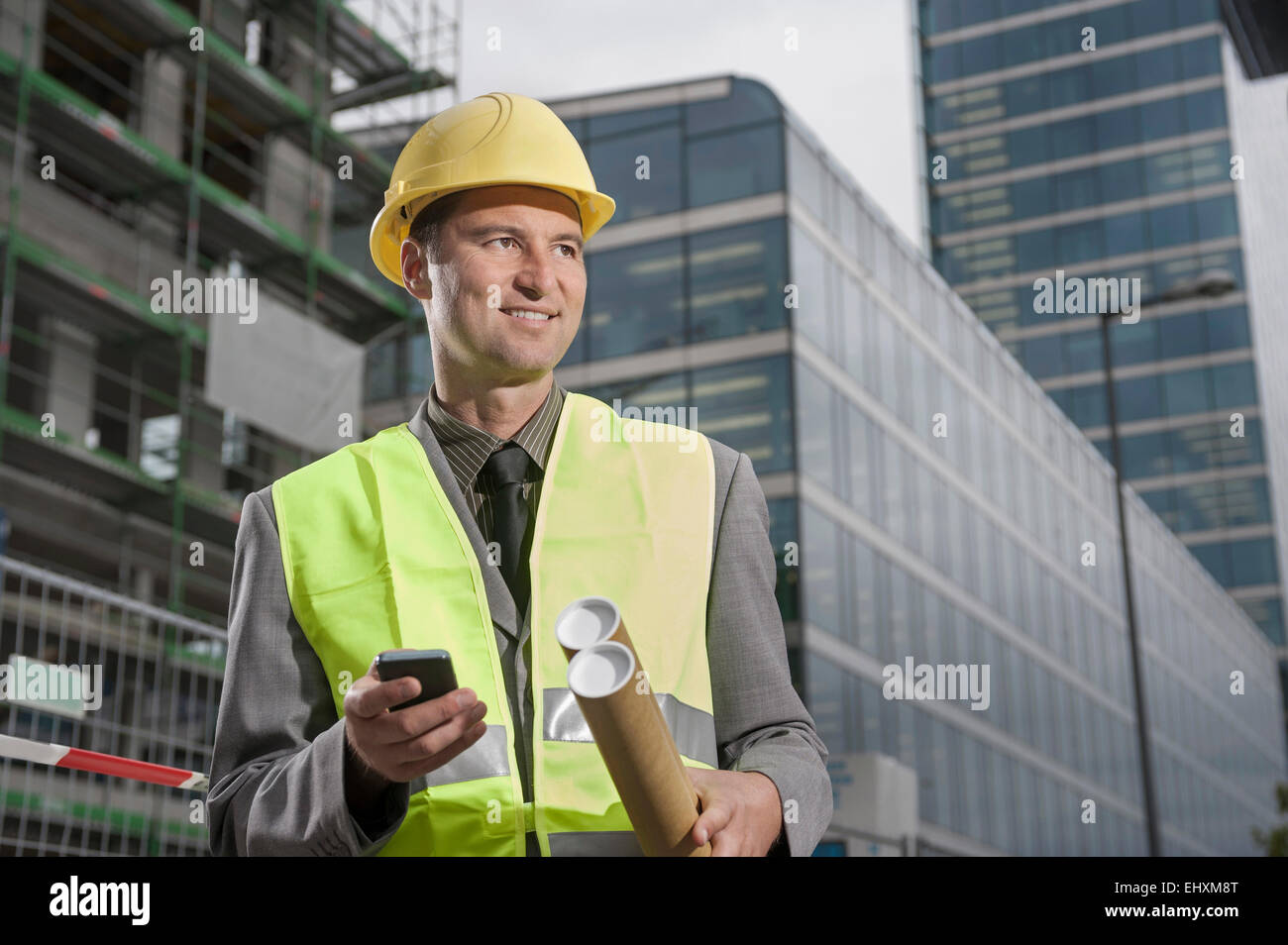 Happy site manager holding blueprints and mobile standing at a ...