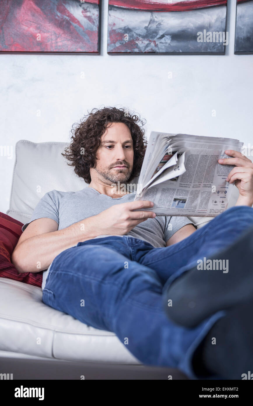 Man lying down on couch and reading a newspaper, Munich, Bavaria ...
