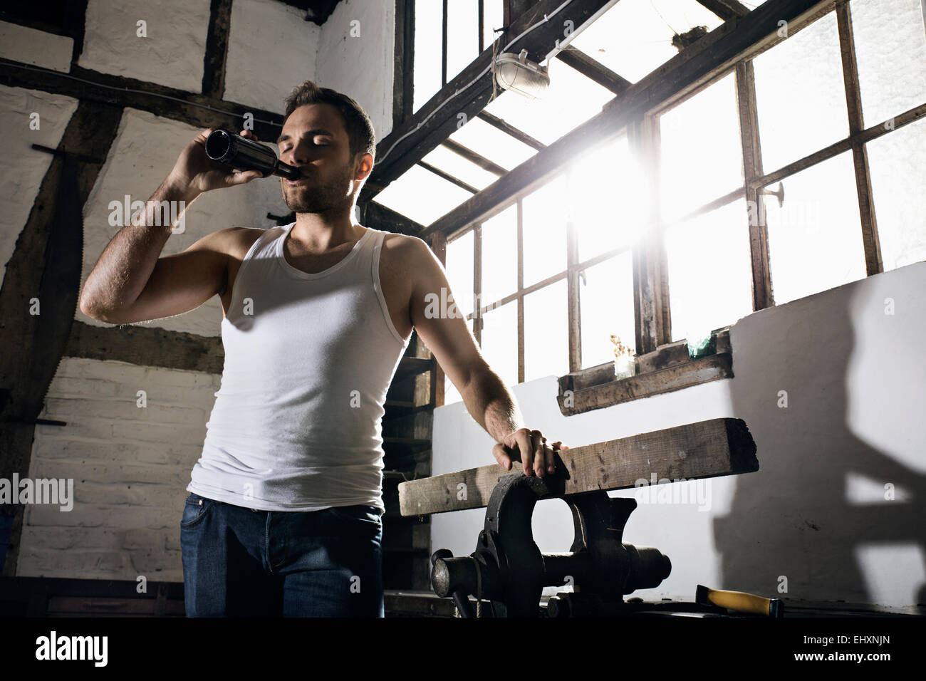 Young man drinking beer in front of his half-timbered house at night ...
