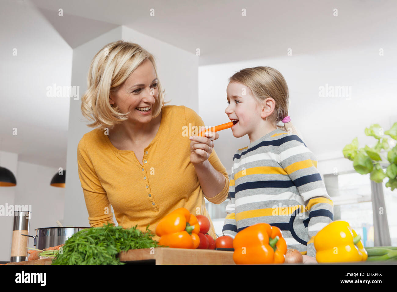 Mother with daughter eating carrot in kitchen Stock Photo - Alamy