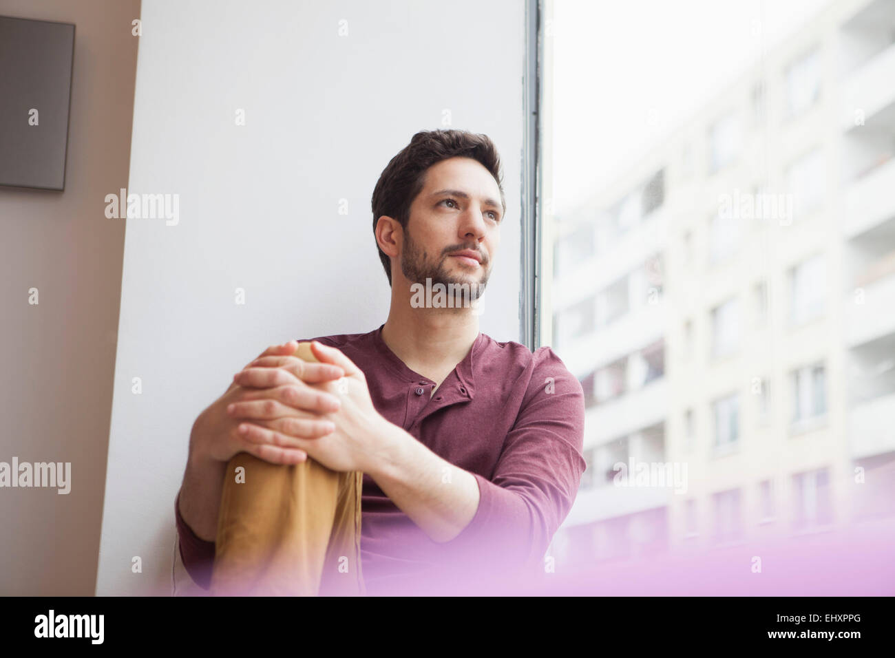 Portrait of man hugging knee looking through window Stock Photo - Alamy