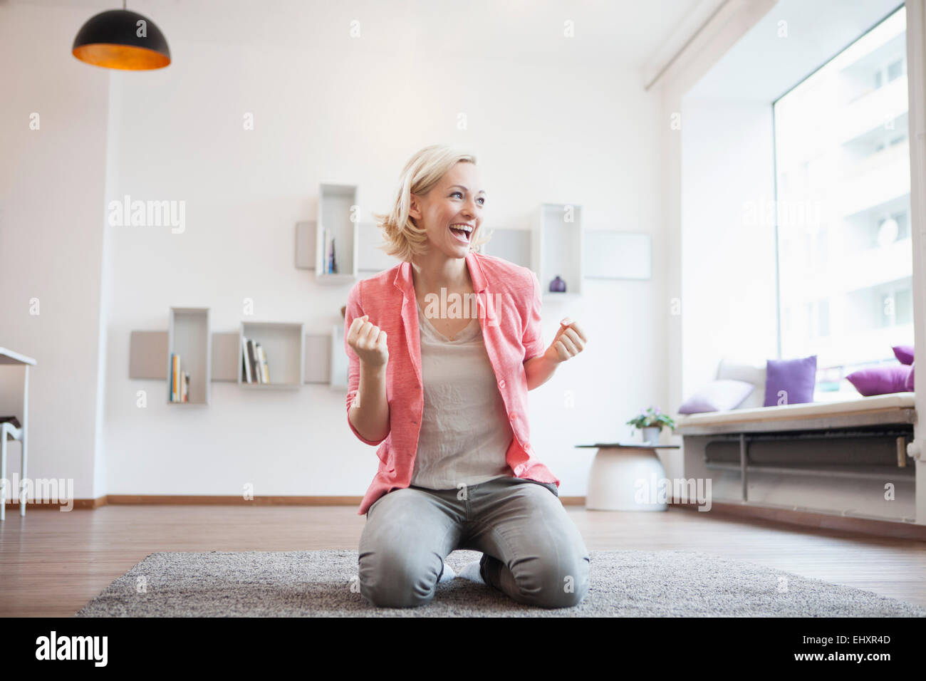Cheering woman sitting on carpet at living room Stock Photo - Alamy