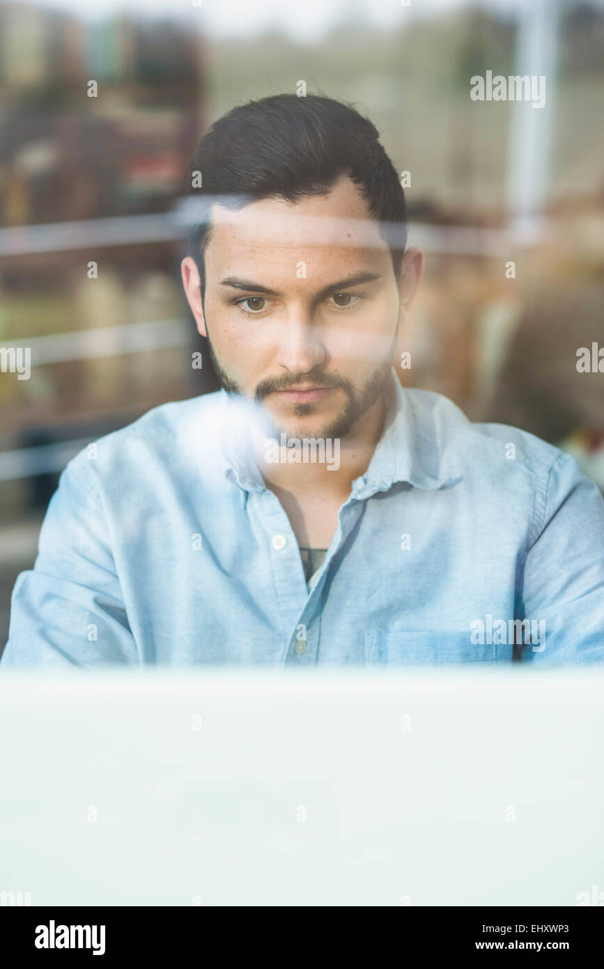 Young man behind windowpane working at computer Stock Photo - Alamy