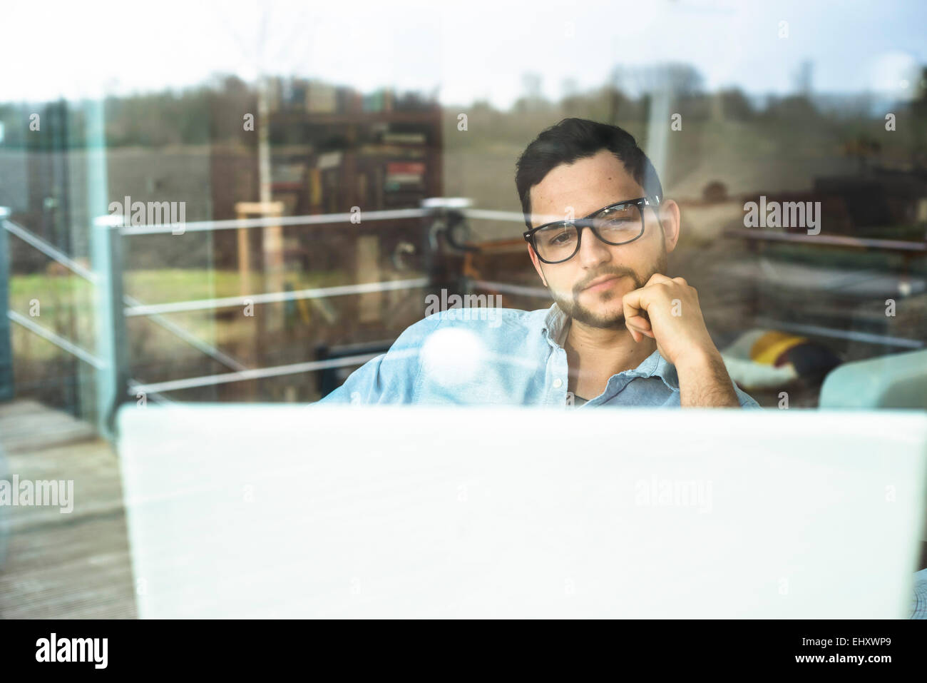 Young man behind windowpane working at computer Stock Photo - Alamy