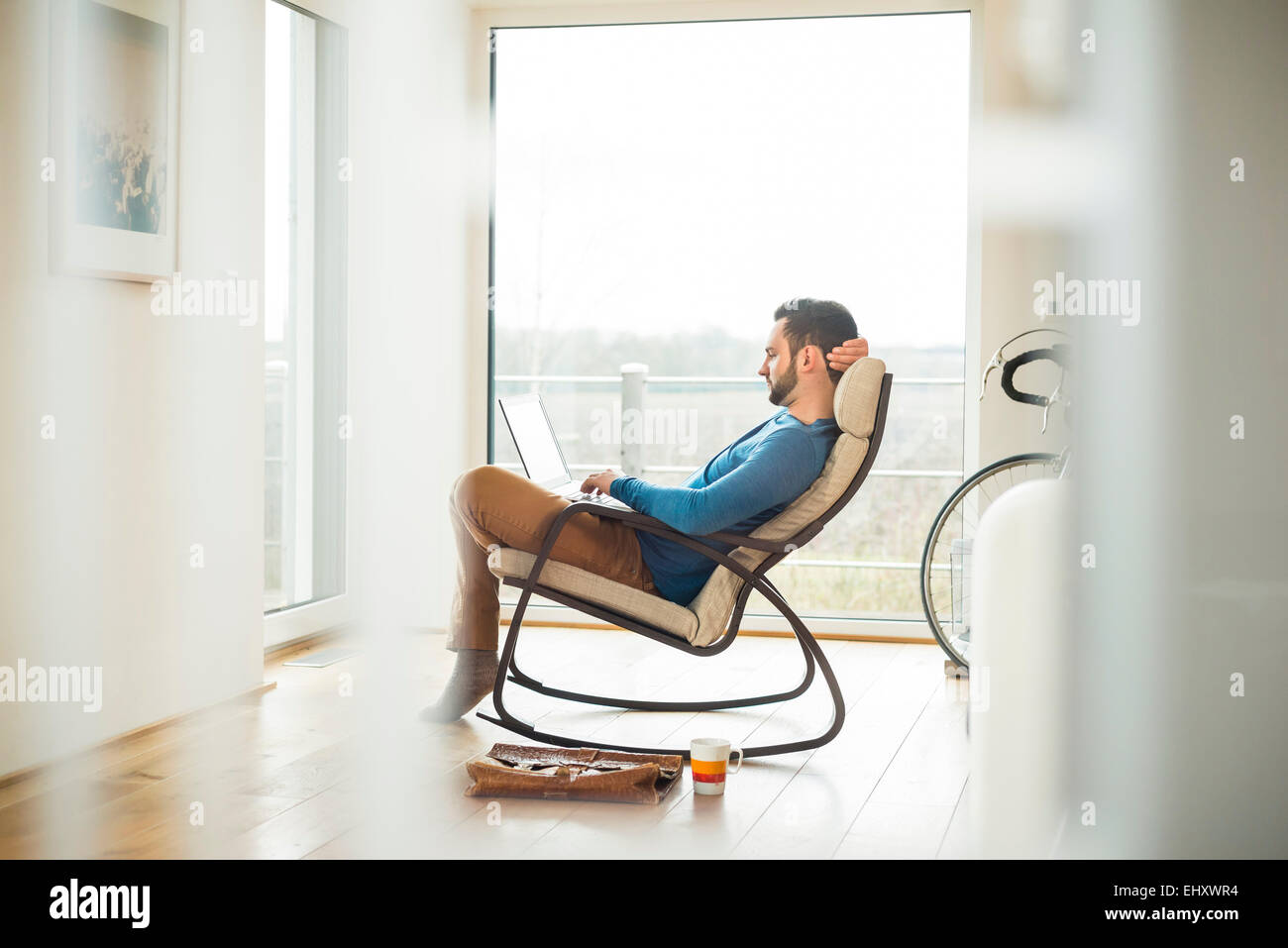 Young man sitting on rocking chair using laptop Stock Photo - Alamy