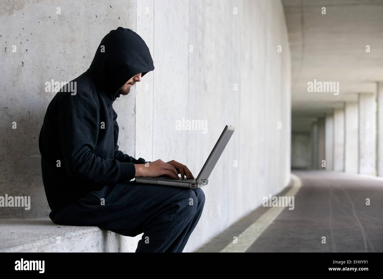 Hacker with laptop sitting in an underground car park Stock Photo - Alamy