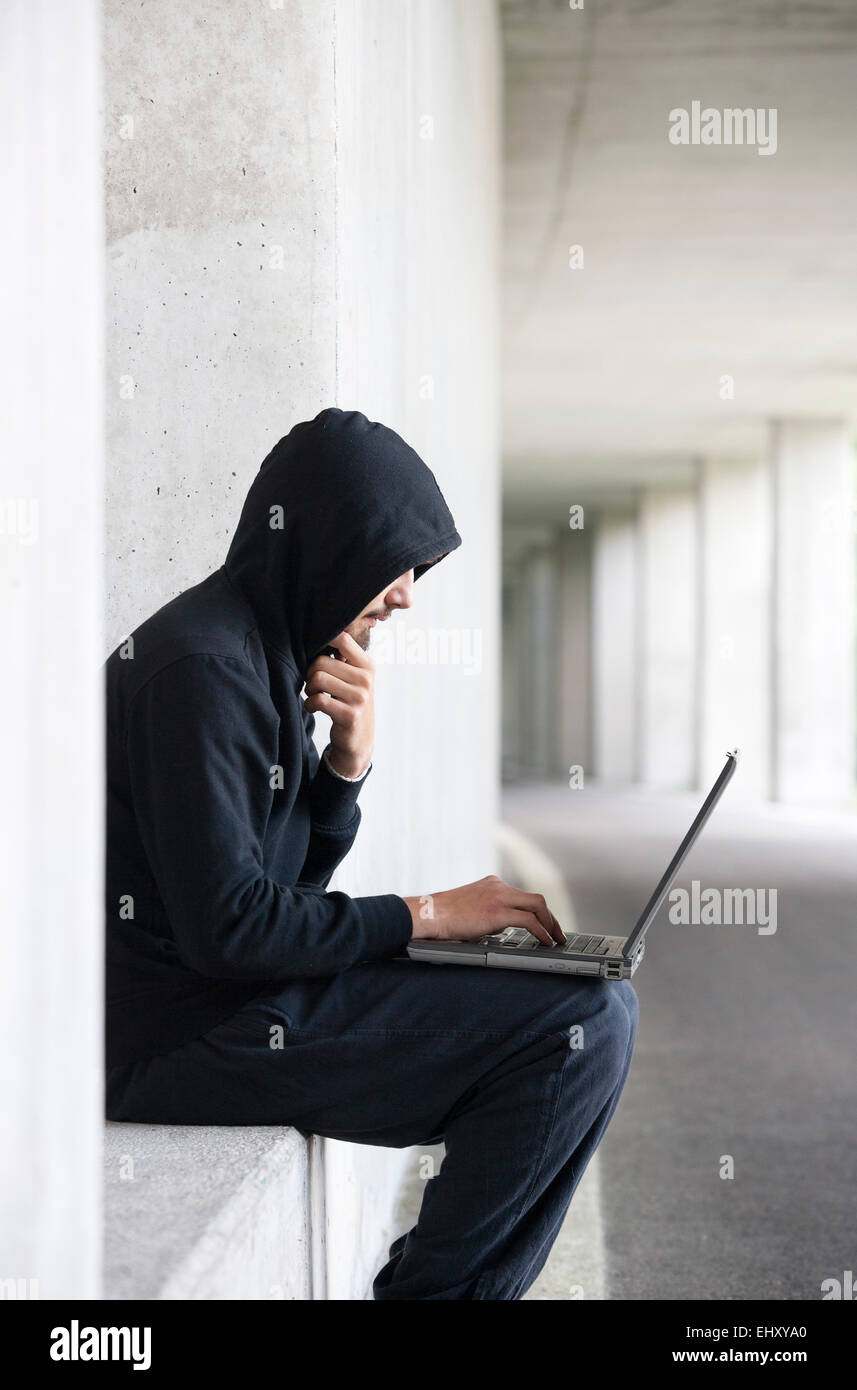Hacker with laptop sitting in an underground car park Stock Photo - Alamy