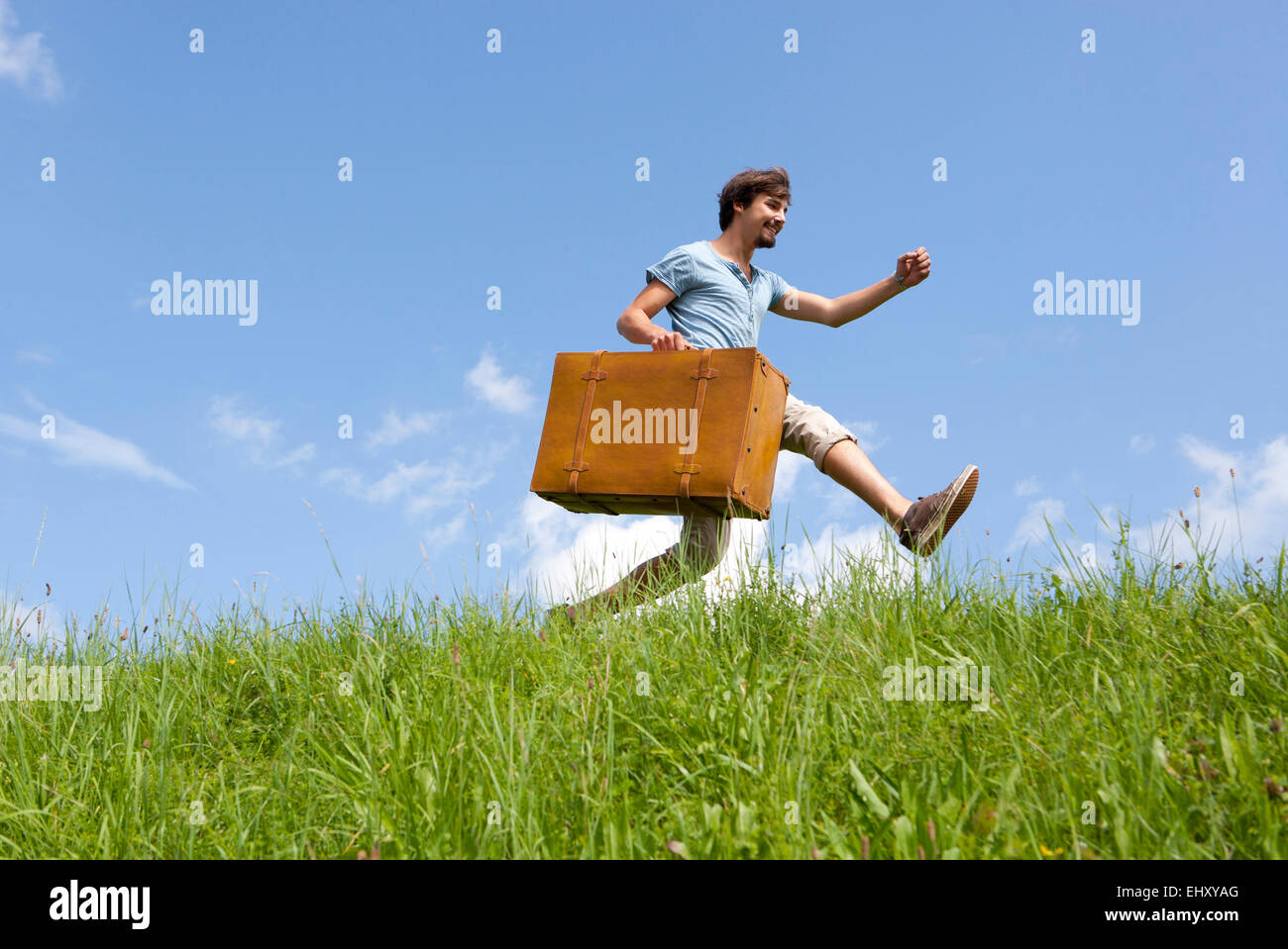 Young man with suitcase running on a meadow Stock Photo - Alamy