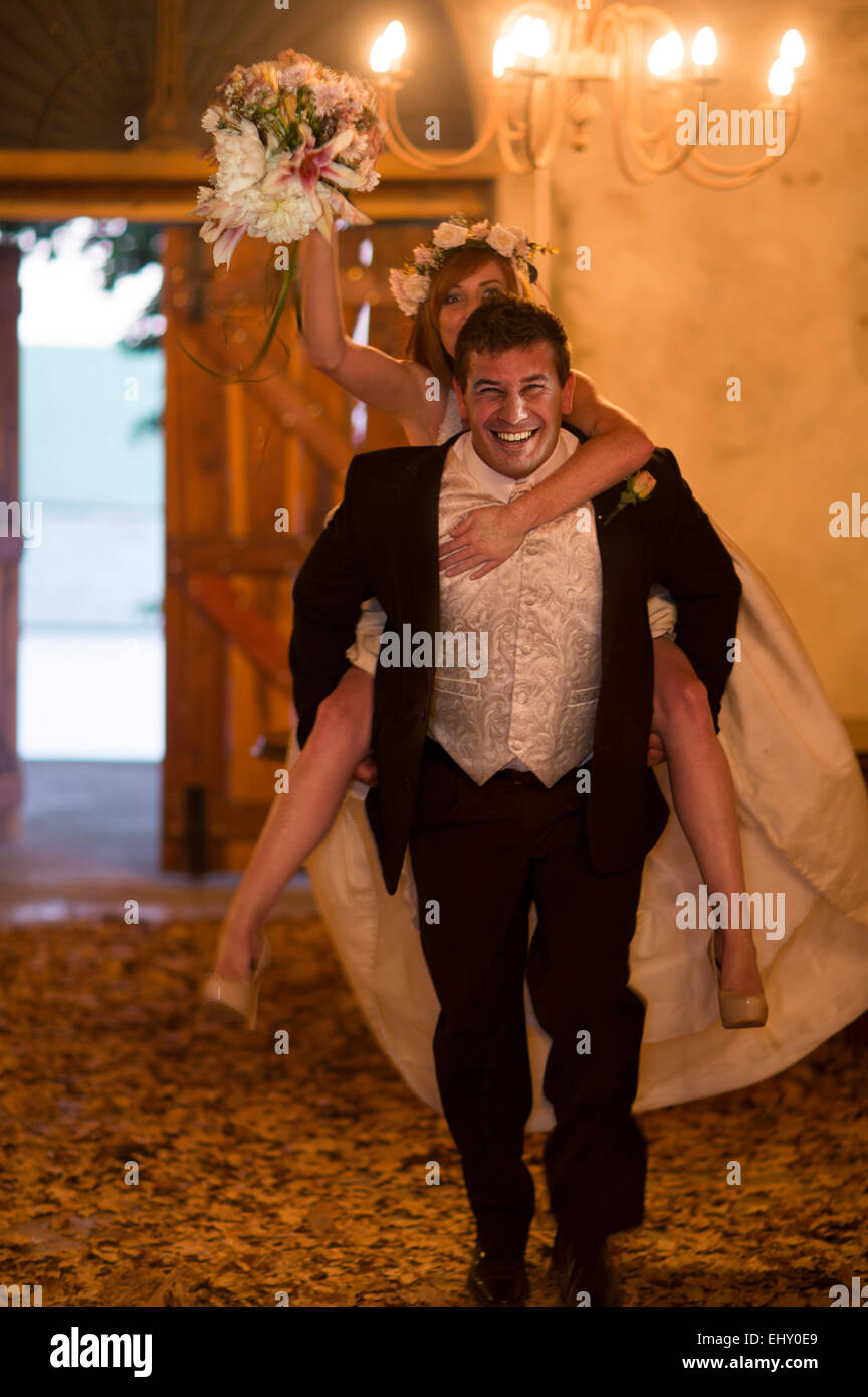 Happy groom carrying bride piggyback in lobby Stock Photo - Alamy