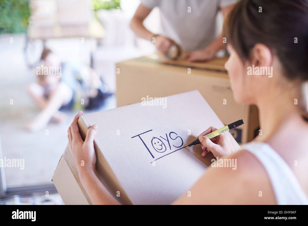 Family moving house, woman writing on box Stock Photo - Alamy