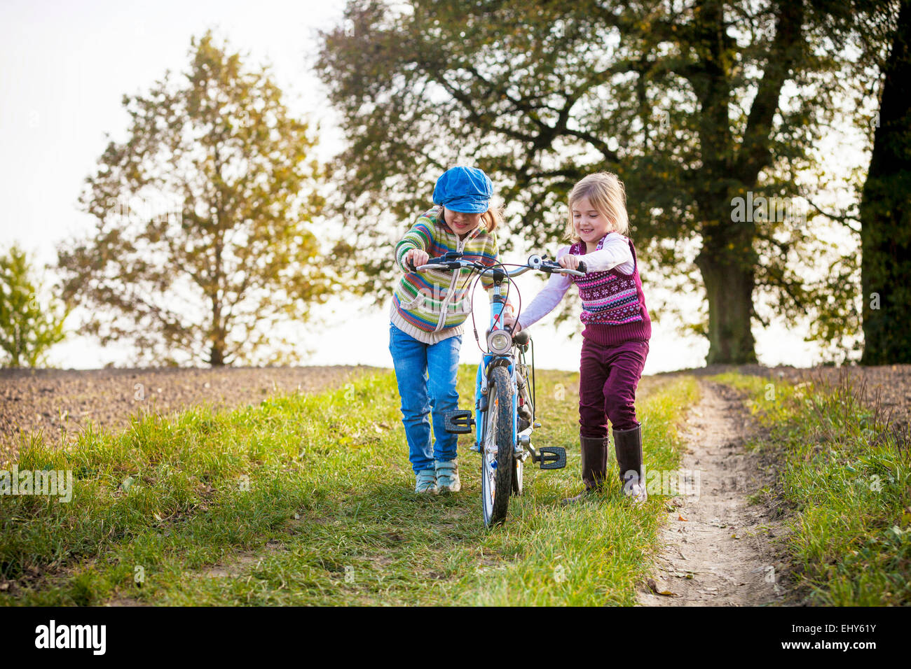 Two girls pushing bicycle on farm track Stock Photo - Alamy