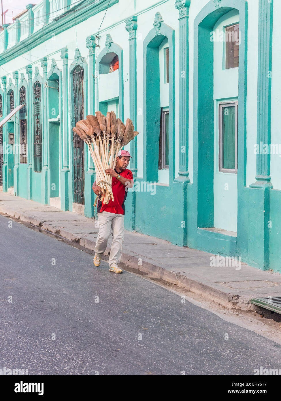 A Hispanic broom salesman carries about a dozen brooms as he walks in ...
