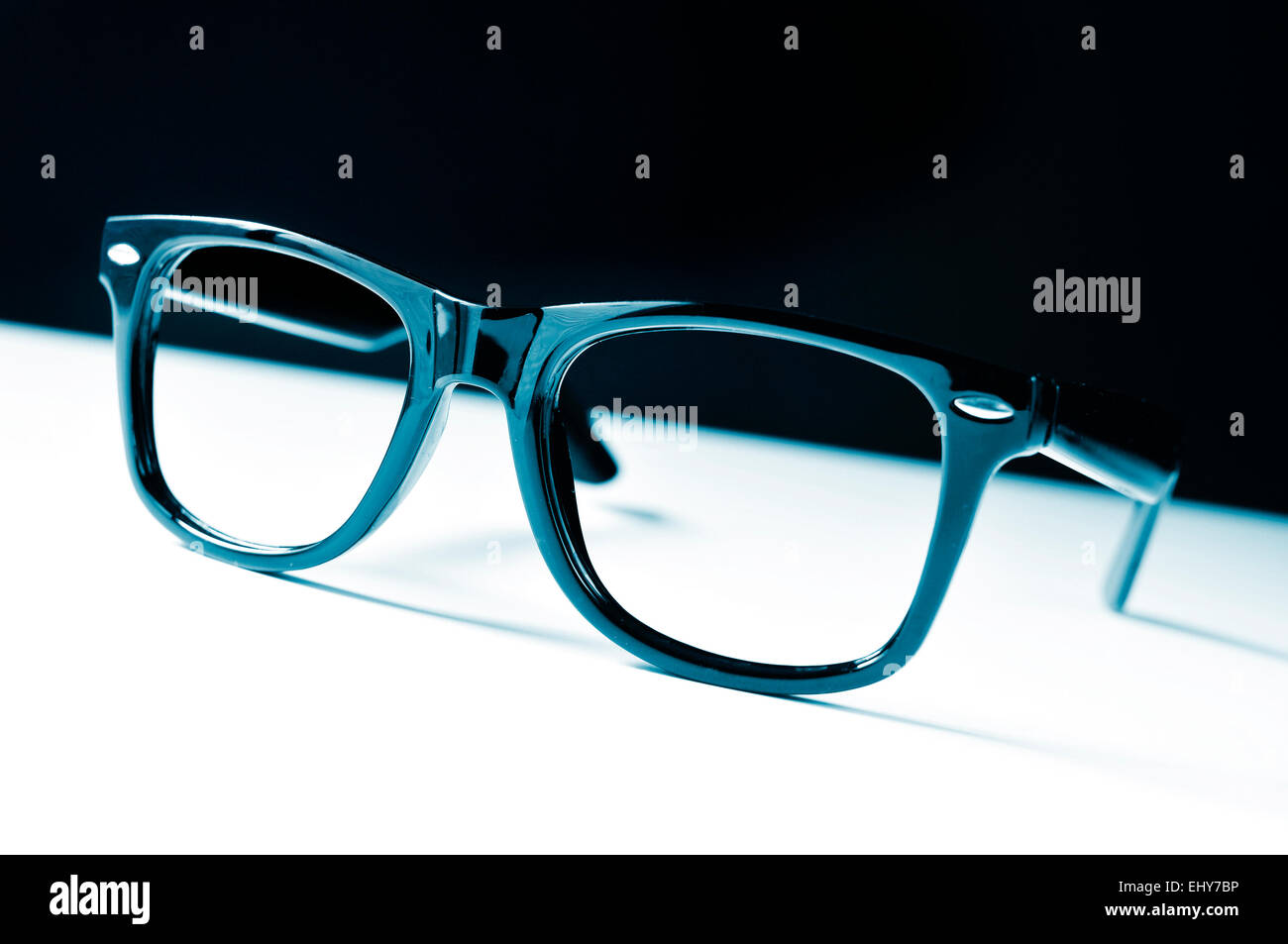 a pair of black plastic-rimmed eyeglasses on a white surface, and a ...