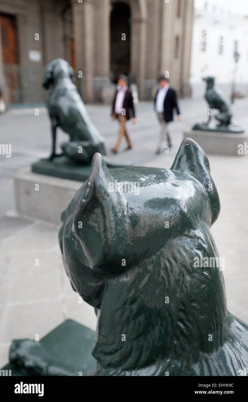 Two people walk past bronze statues of dogs guard the Plaza Santa Ana ...