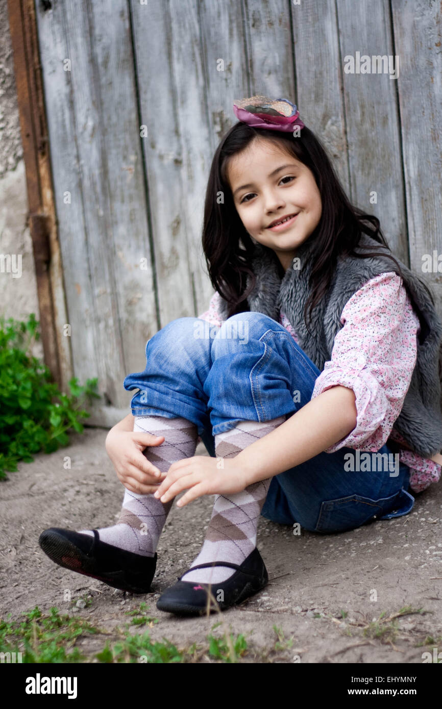 Girl sitting on ground leaning against wooden fence Stock Photo - Alamy