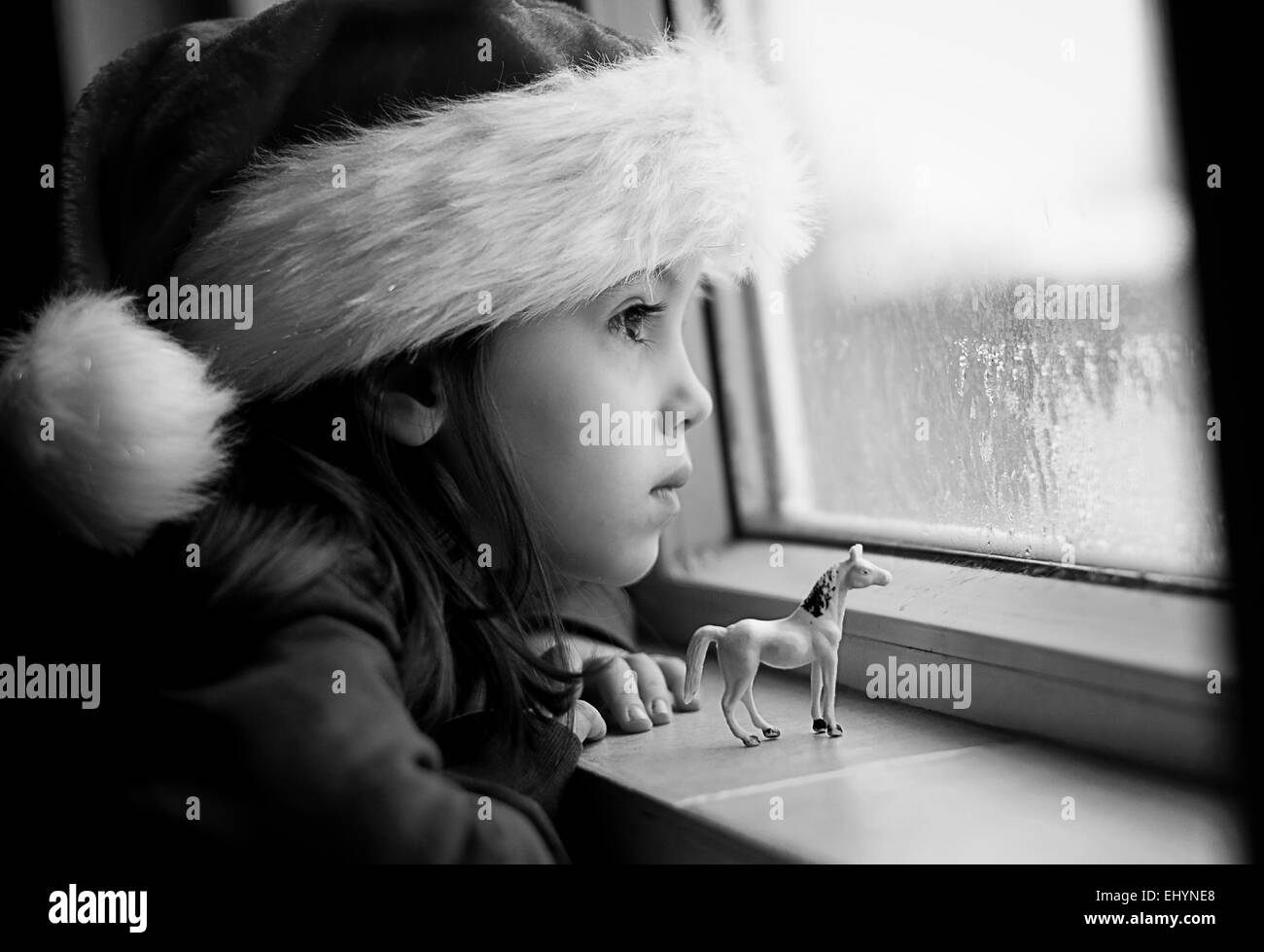 Girl wearing a Christmas hat looking out of the window Stock Photo - Alamy