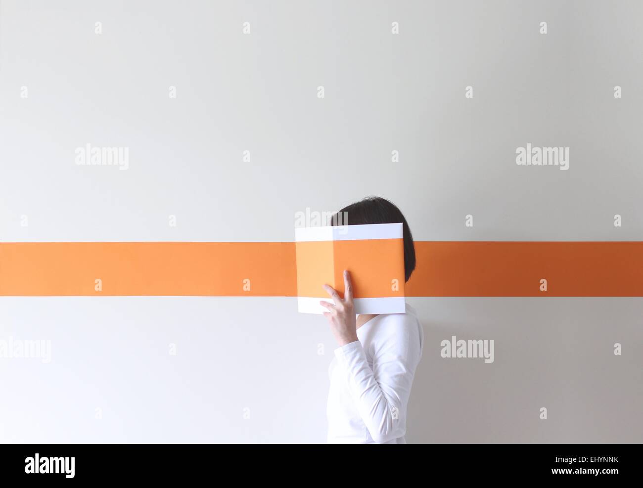 Side view of a woman hiding her face behind a book with an orange ...