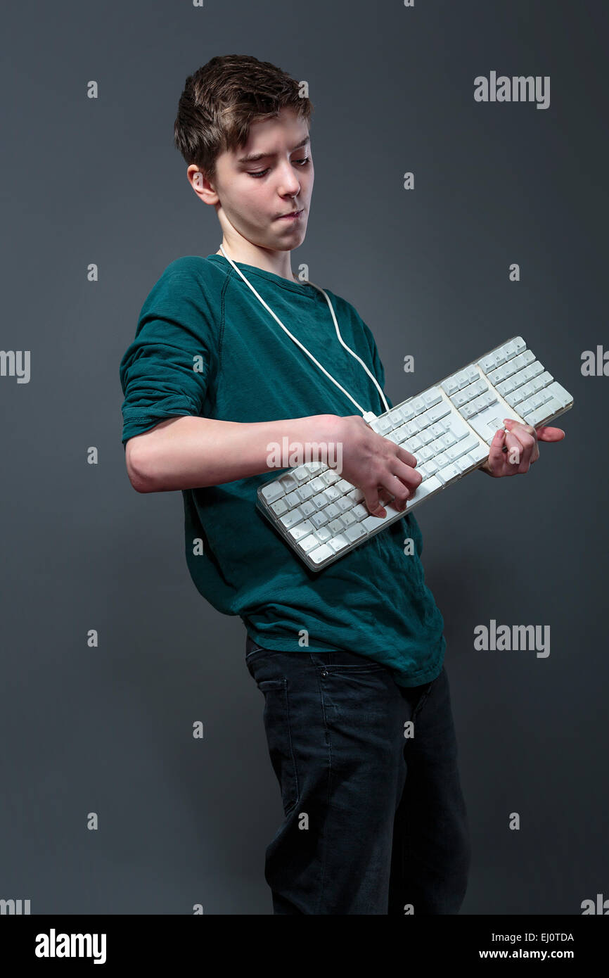 teenage boy using a computer keyboard like a piano, isolated on gray ...