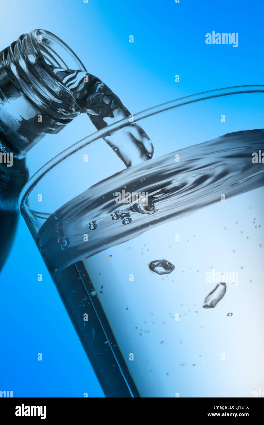 pouring water into glass from a bottle, on blue background Stock Photo - Alamy