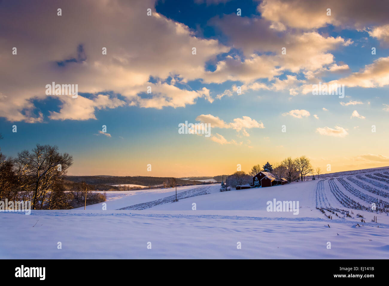 View of snow covered farm fields and rolling hills at sunset in rural ...