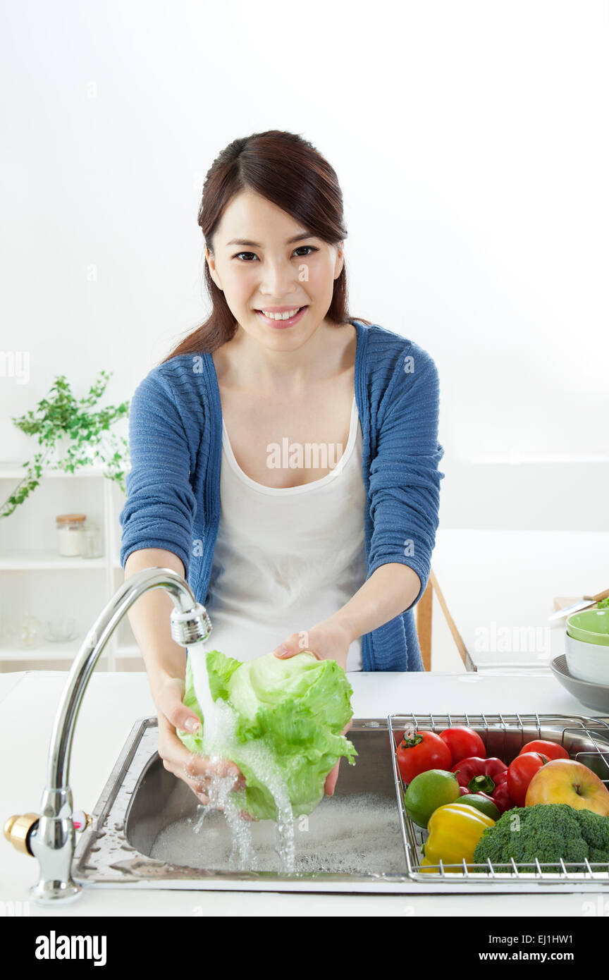 Young woman washing vegetables in the kitchen sink and smiling at the ...