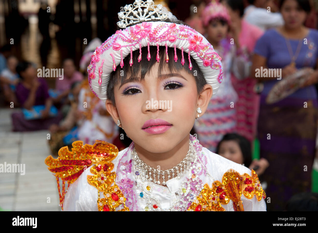 A young Burmese boy dressed in colourful robes and doll like make up ...