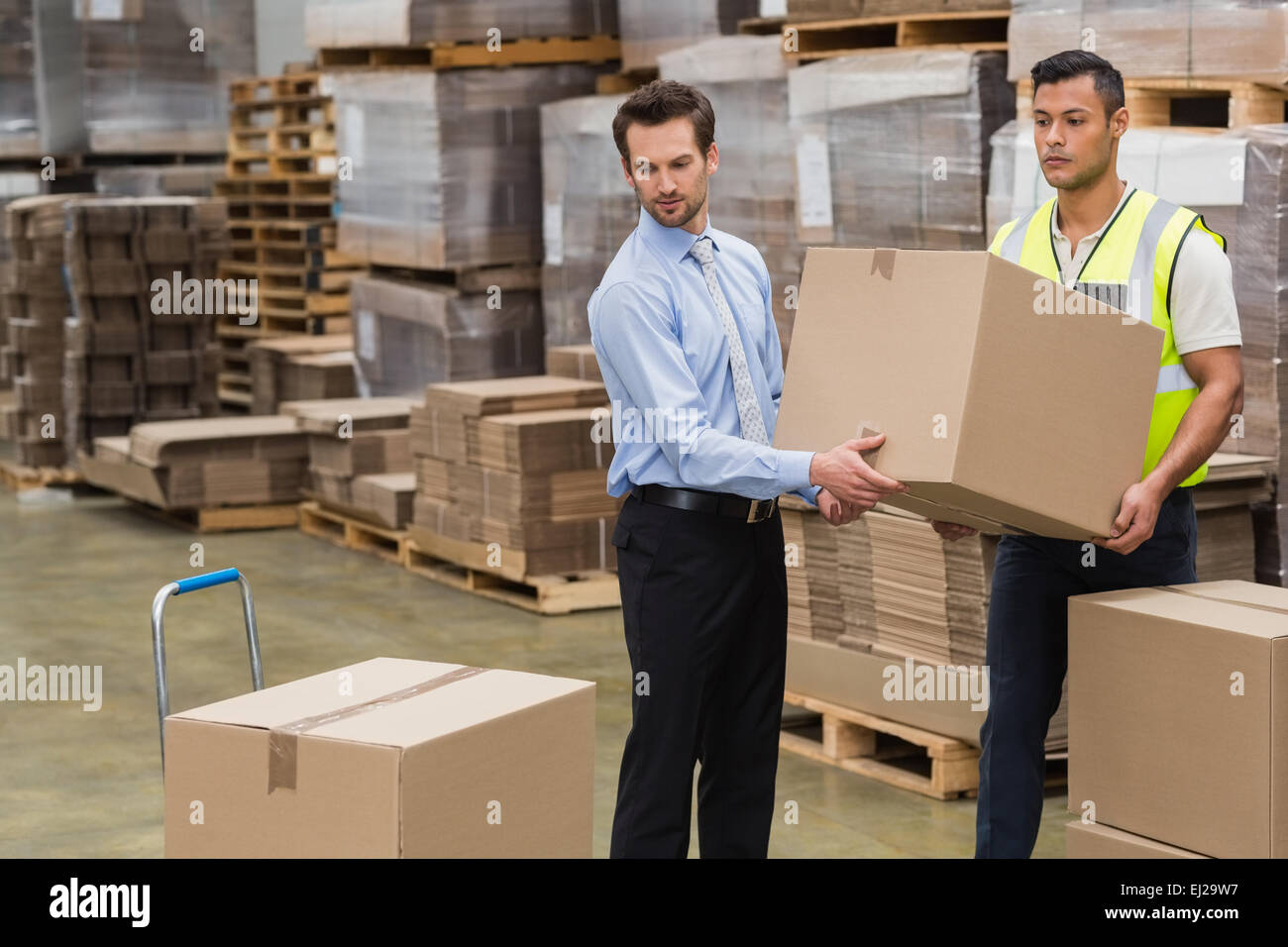 Warehouse worker and manager carrying a box together Stock Photo - Alamy