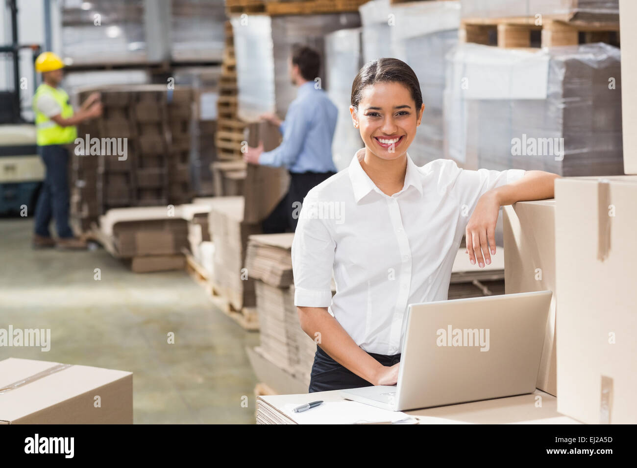 Smiling warehouse manager using laptop Stock Photo - Alamy