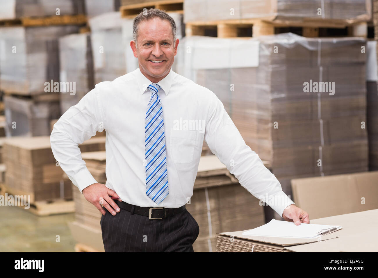 Smiling boss leaning on stack of cartons Stock Photo - Alamy