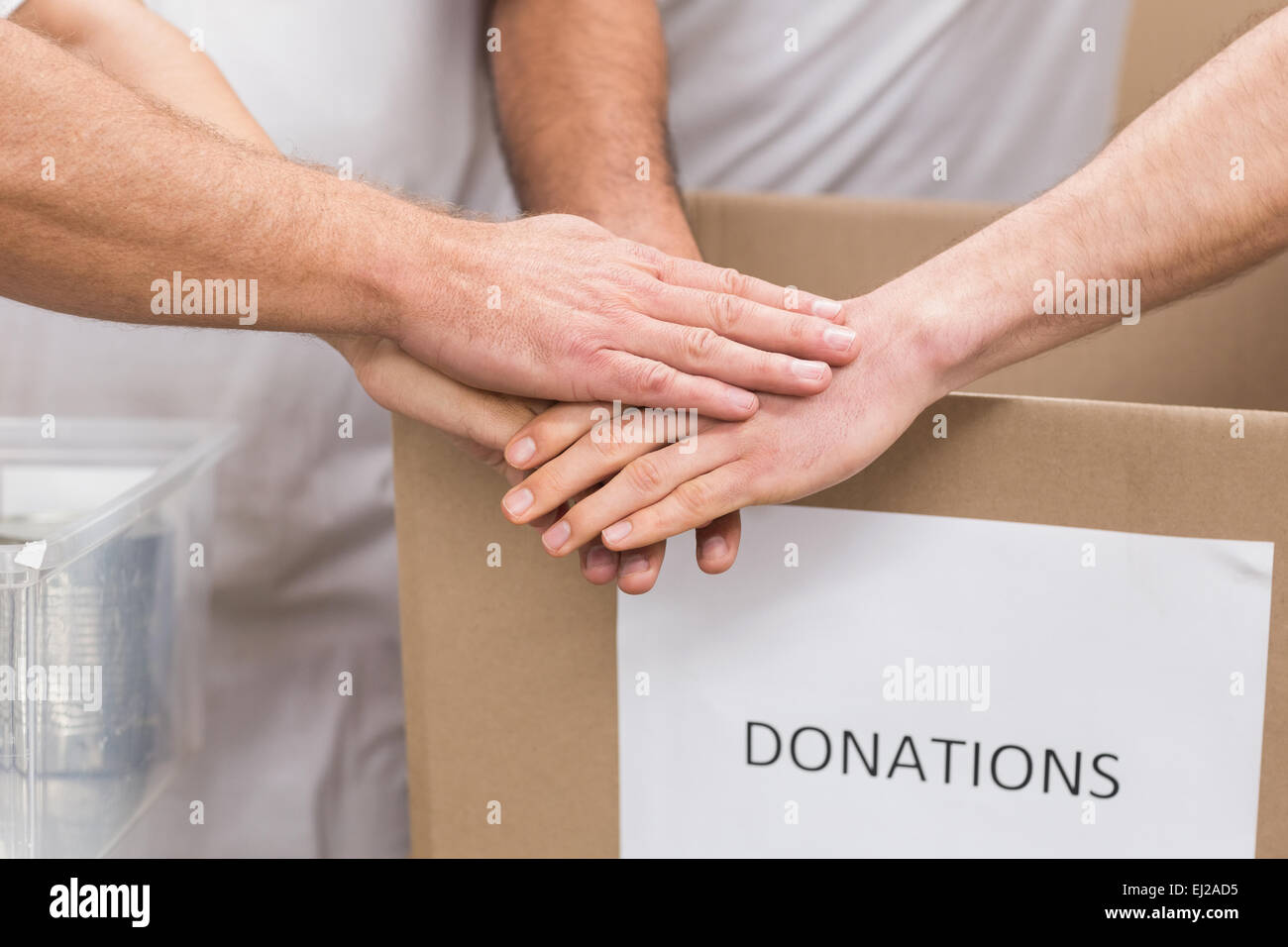 Volunteer team holding hands on a box of donations Stock Photo - Alamy