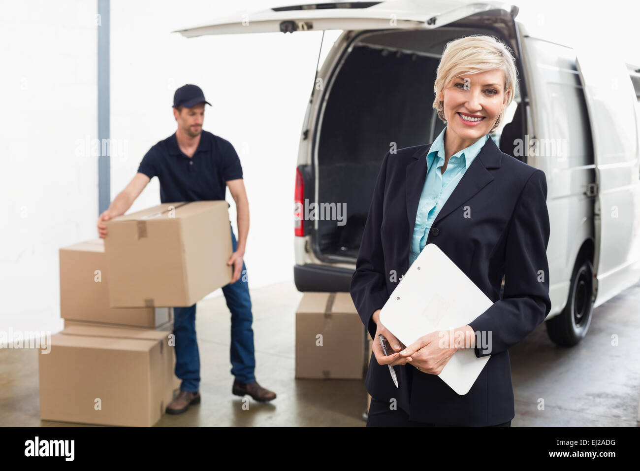 Delivery driver packing his van with manager smiling Stock Photo - Alamy