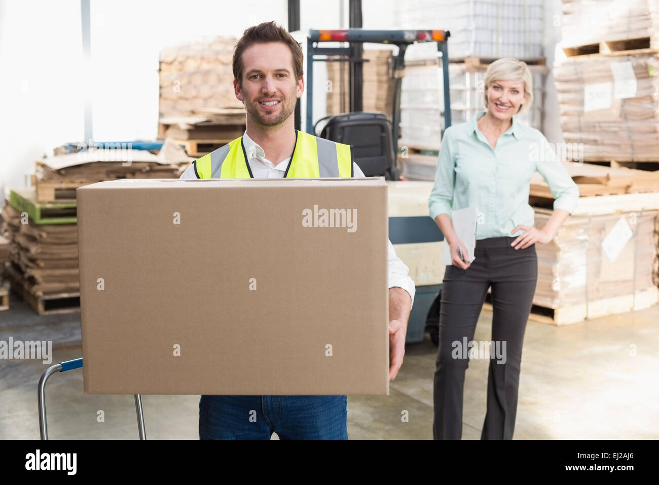 Smiling warehouse worker carrying box Stock Photo - Alamy