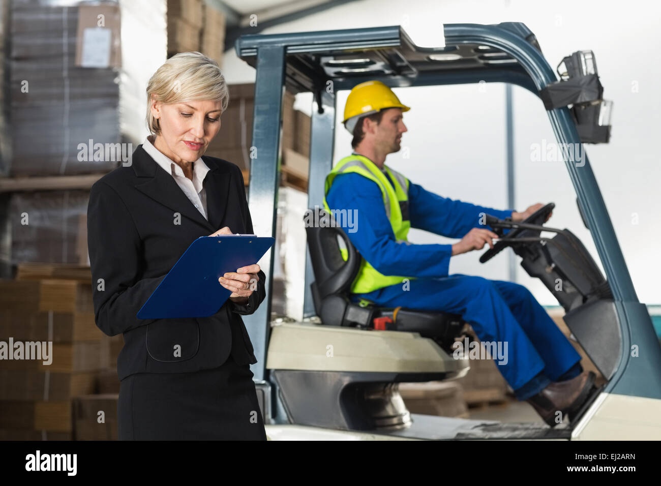 Manager writing on clipboard in front of her colleague Stock Photo - Alamy