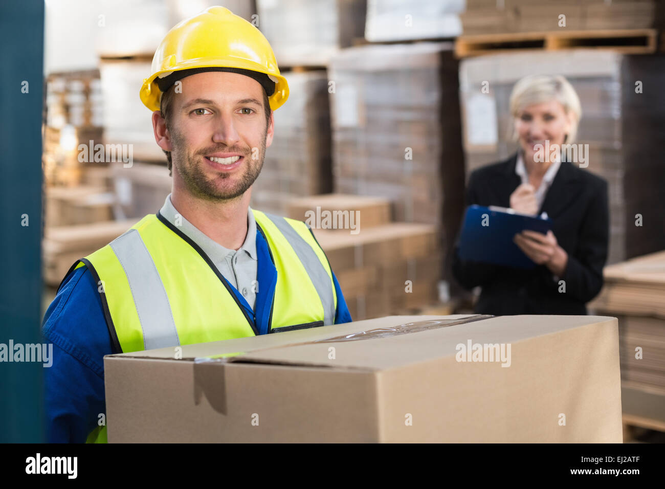 Warehouse worker holding box with manager behind him Stock Photo - Alamy