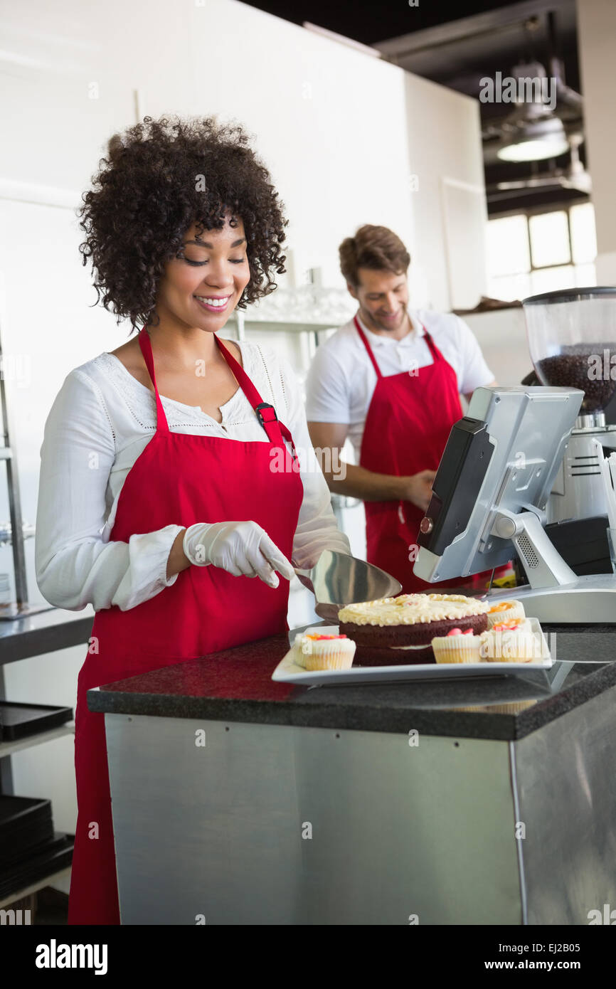 Pretty waitress slicing cake with waiter behind her Stock Photo - Alamy