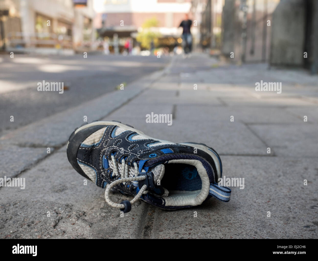 A lost children´s shoe on the pavement with a man approaching in the ...
