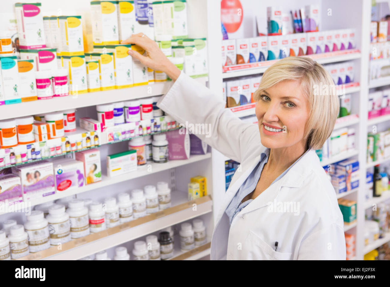 Smiling pharmacist taking box from shelf Stock Photo - Alamy