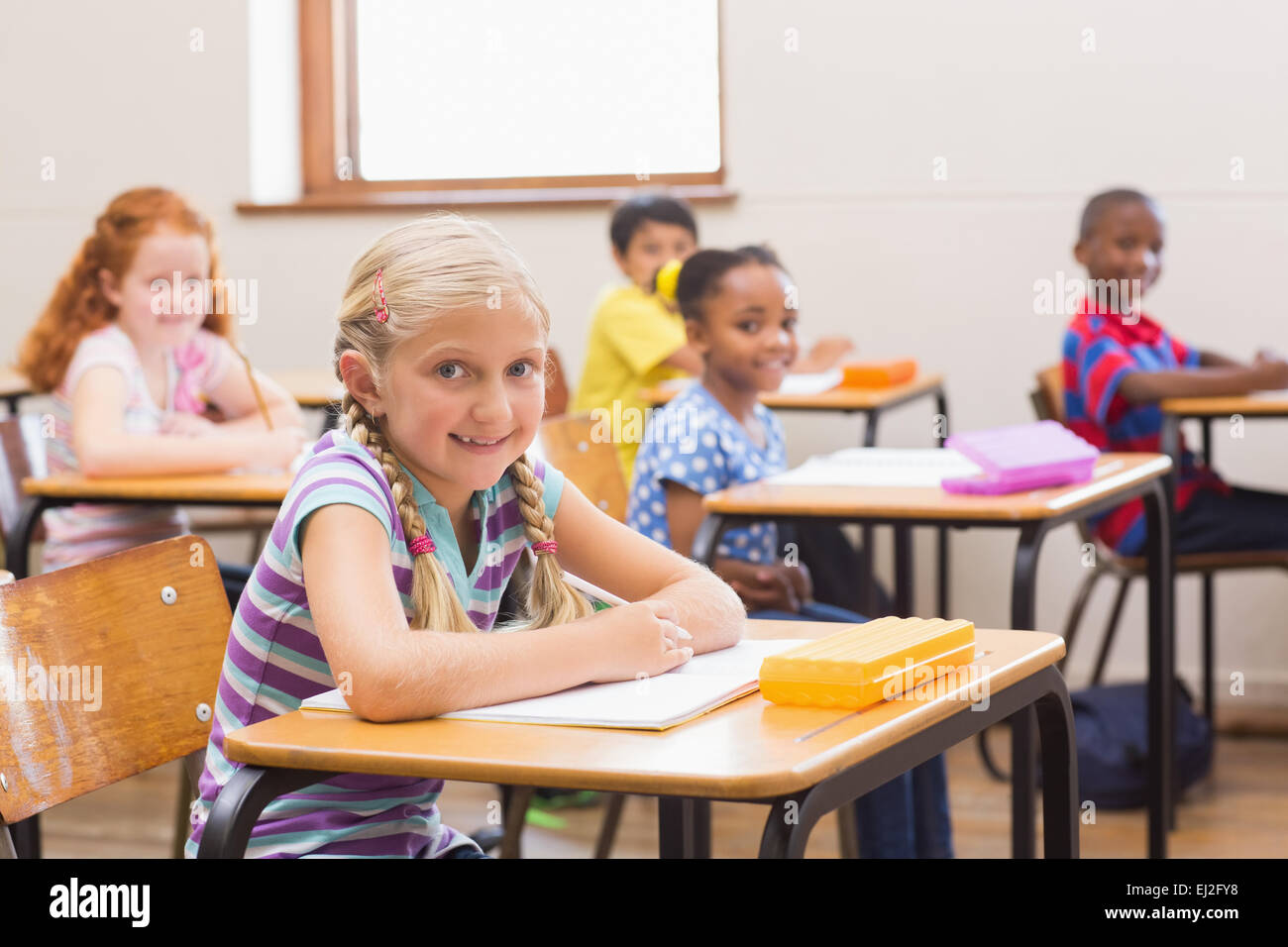 Smiling pupils sitting at her desk Stock Photo - Alamy