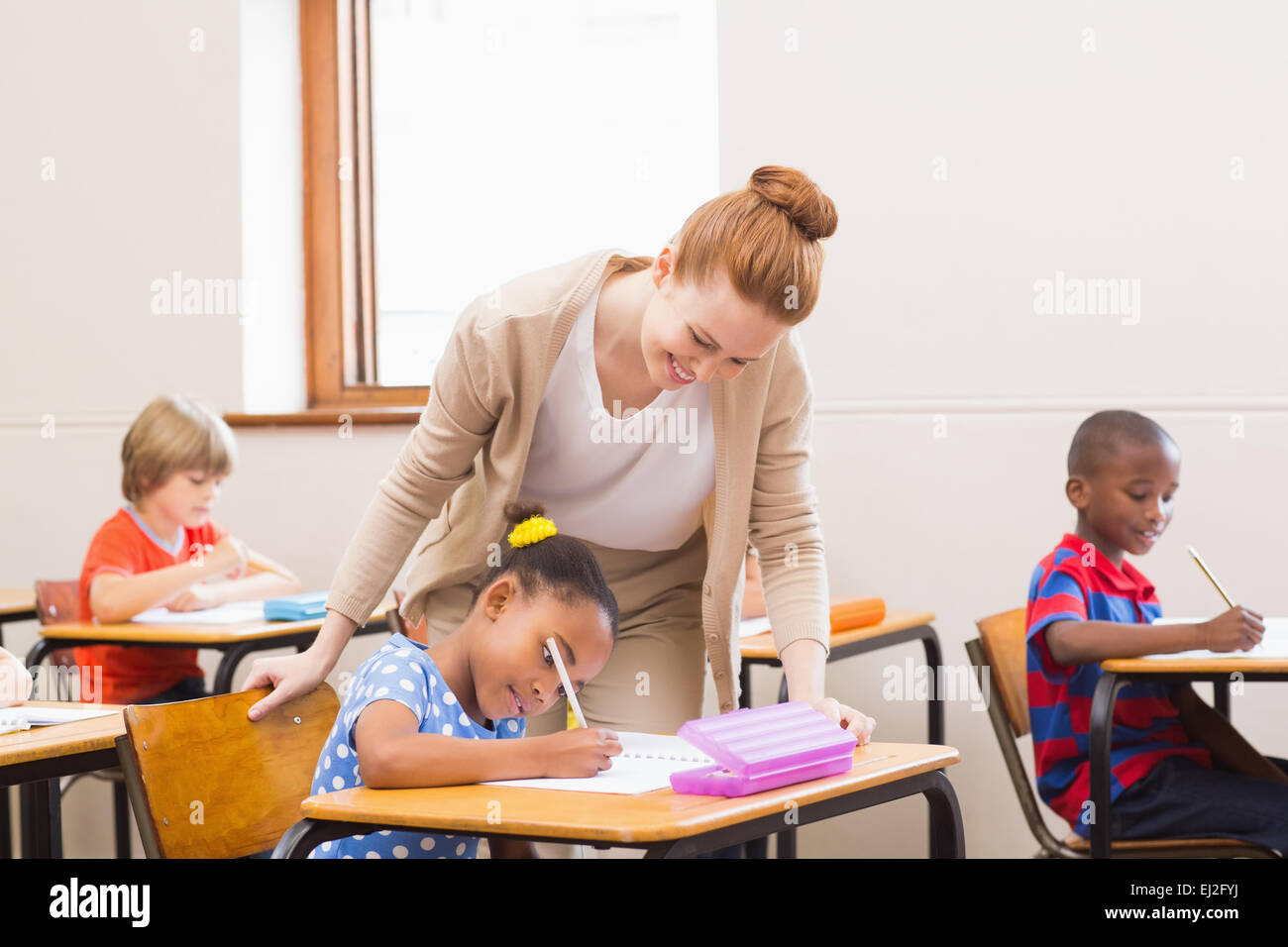 Teacher helping pupil in classroom Stock Photo - Alamy