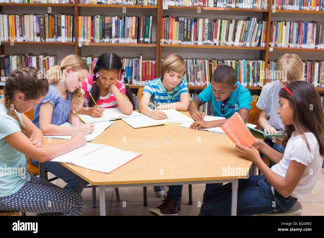 Cute pupils writing at desk in library Stock Photo - Alamy