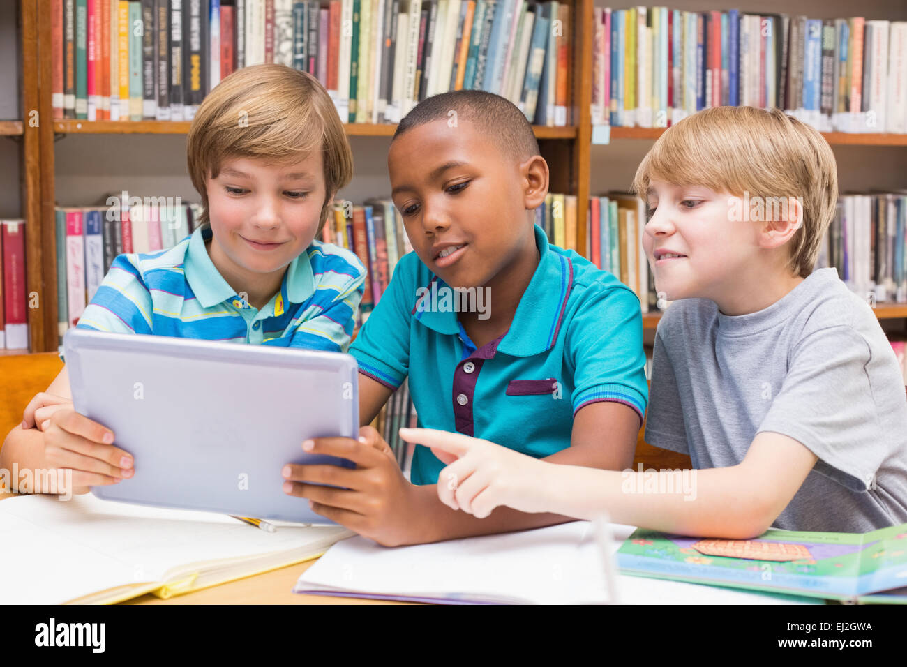 Cute pupils using tablet computer in library Stock Photo - Alamy