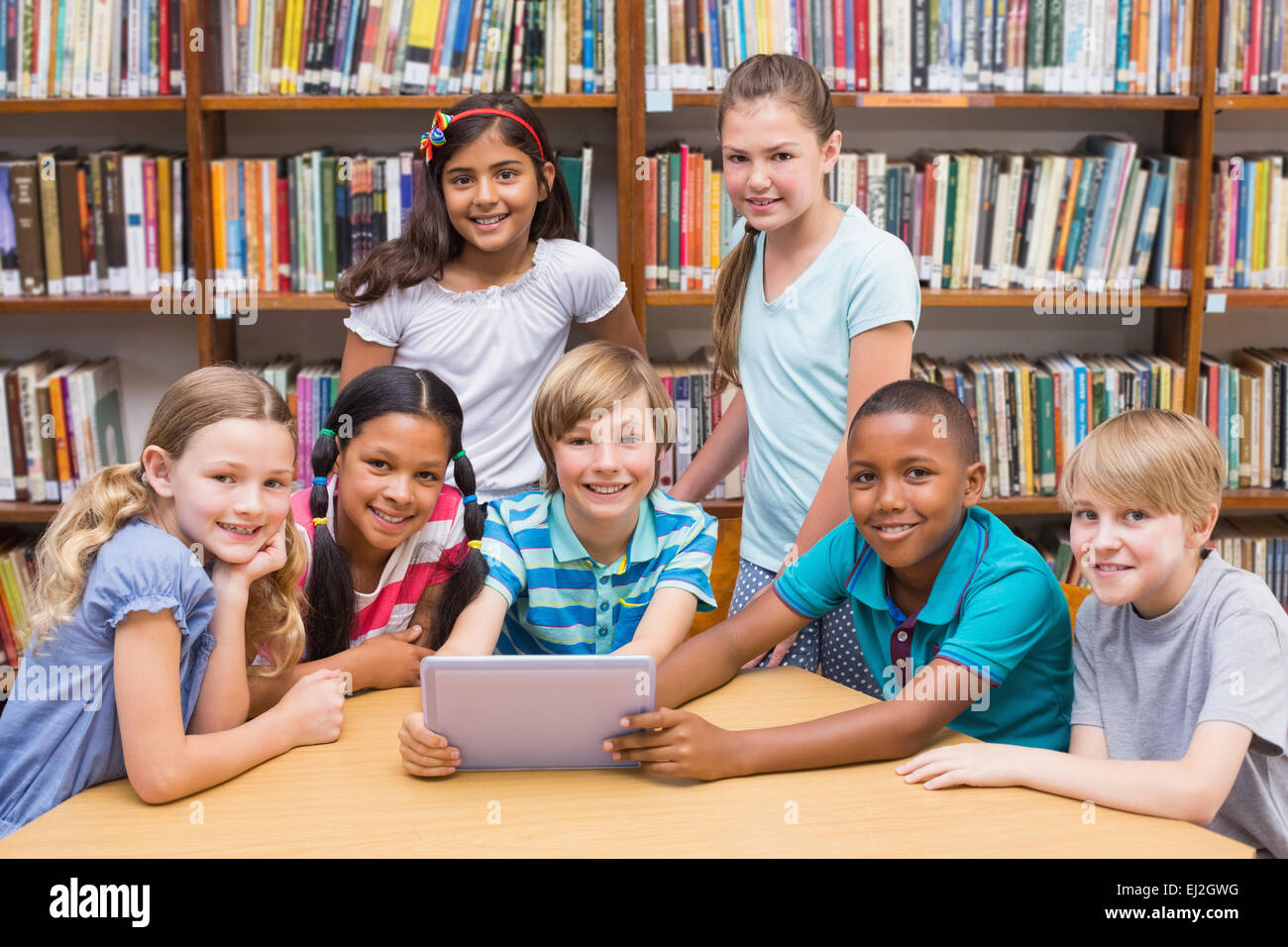 Cute pupils using tablet computer in library Stock Photo - Alamy