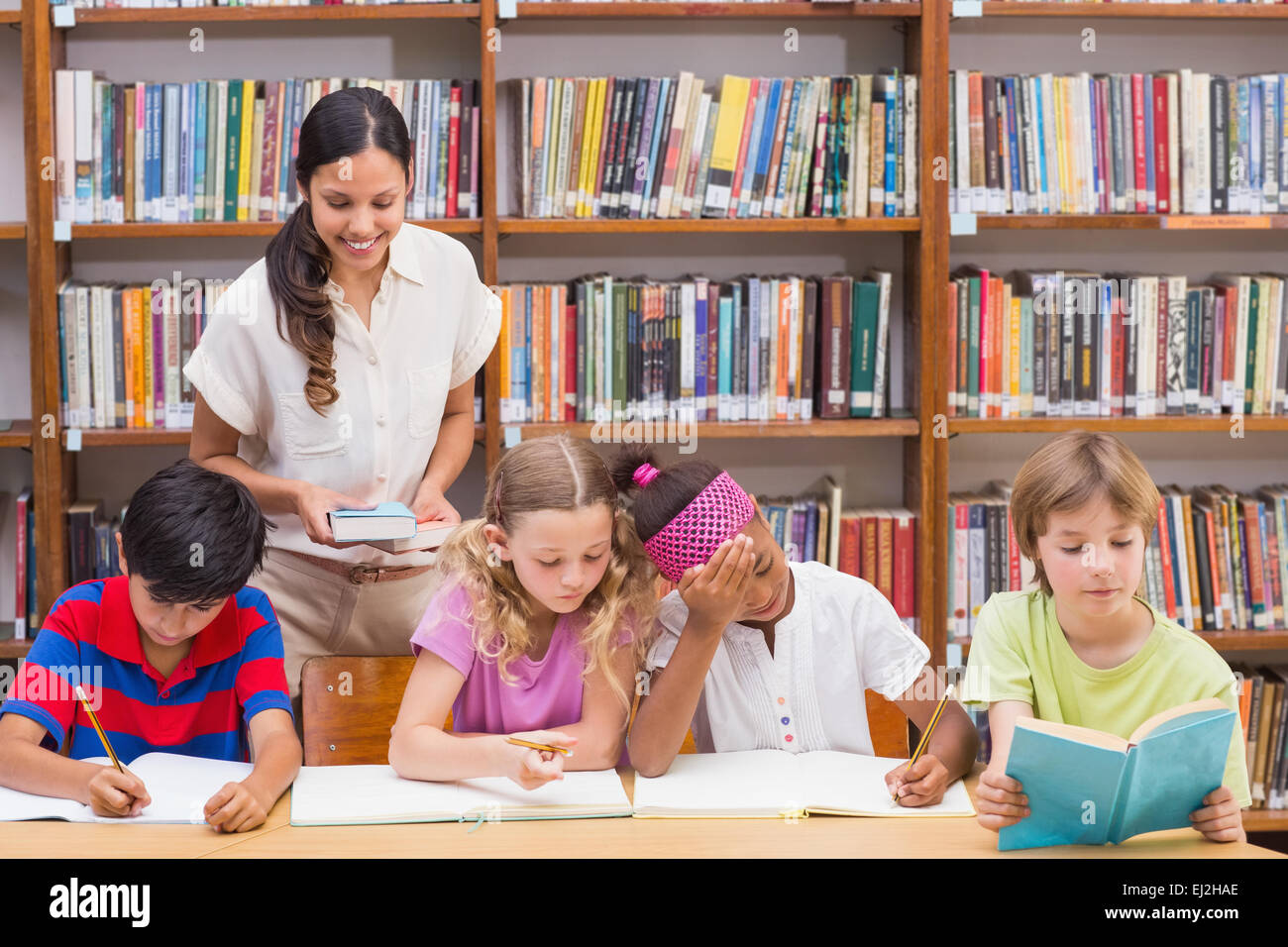 Pretty teacher helping pupils in library Stock Photo - Alamy