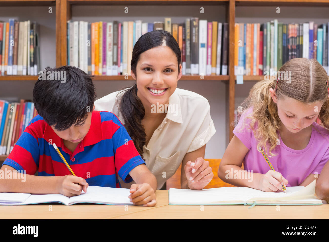 Pretty teacher helping pupils in library Stock Photo - Alamy