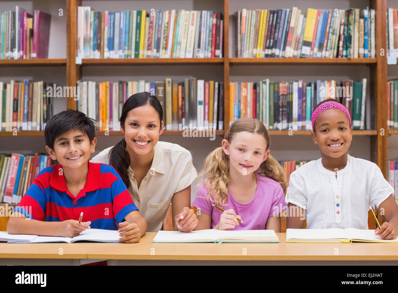 Pretty teacher helping pupils in library Stock Photo - Alamy